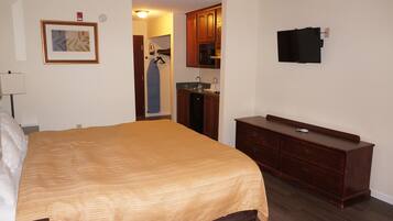 Quarto com cama, penteadeira, televisão e cozinha.
