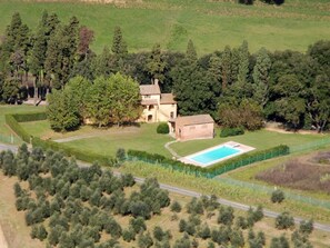 Uma casa grande com piscina, rodeada por um gramado bem cuidado e árvores.