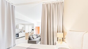Quarto de hotel moderno com uma cama grande, um sofá, uma escrivaninha e vista para a cozinha e sala de estar.