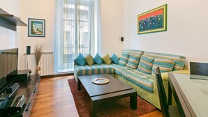 Uma sala de estar com sofá, mesa de centro, televisão e janela com cortinas.