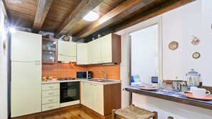 Cozinha compacta com vigas de madeira, micro-ondas, fogão, pia e um pequeno espaço de jantar com duas cadeiras.