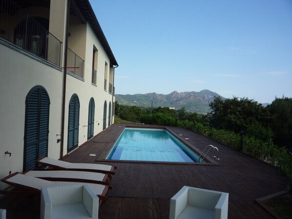 Uma piscina com deck de madeira, mobiliário de exterior e vista para montanhas.