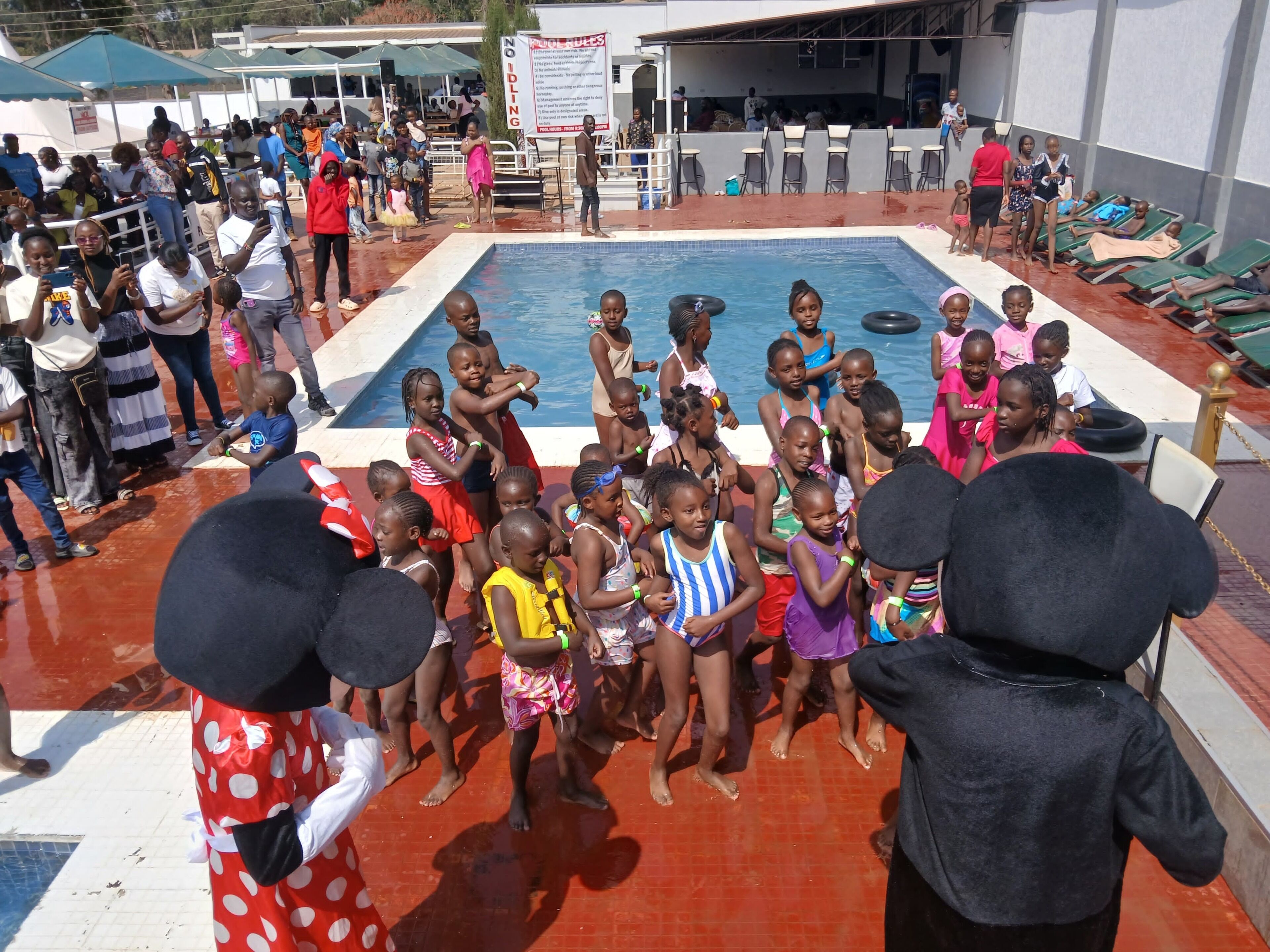 Uma área de piscina com pessoas, incluindo crianças e adultos, reunidas.