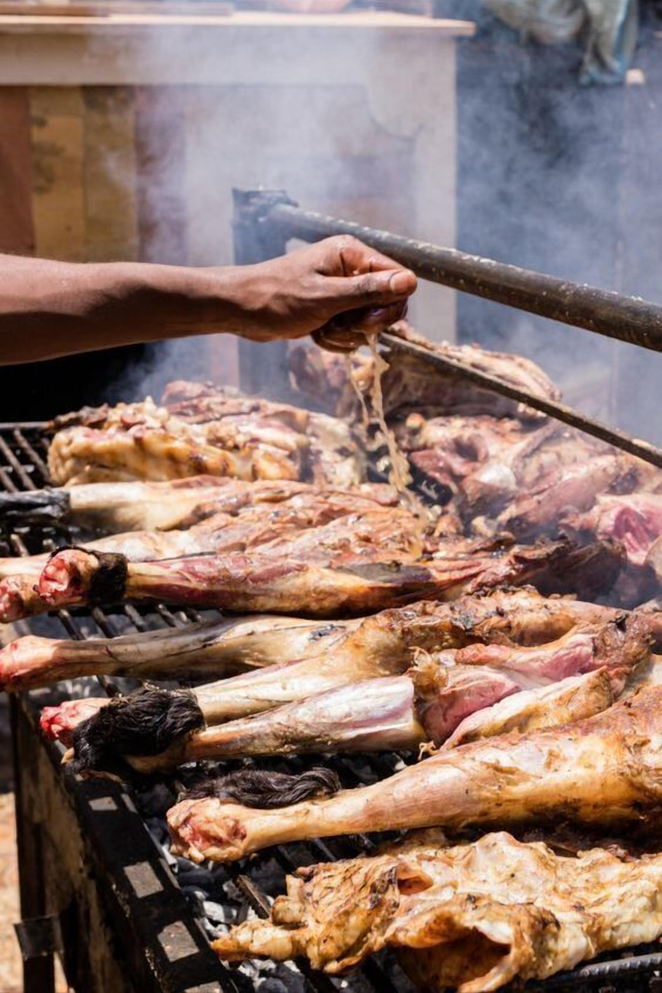 Uma pessoa assando diversos tipos de carne em uma churrasqueira.
