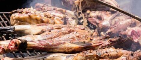 Uma pessoa assando diversos tipos de carne em uma churrasqueira.