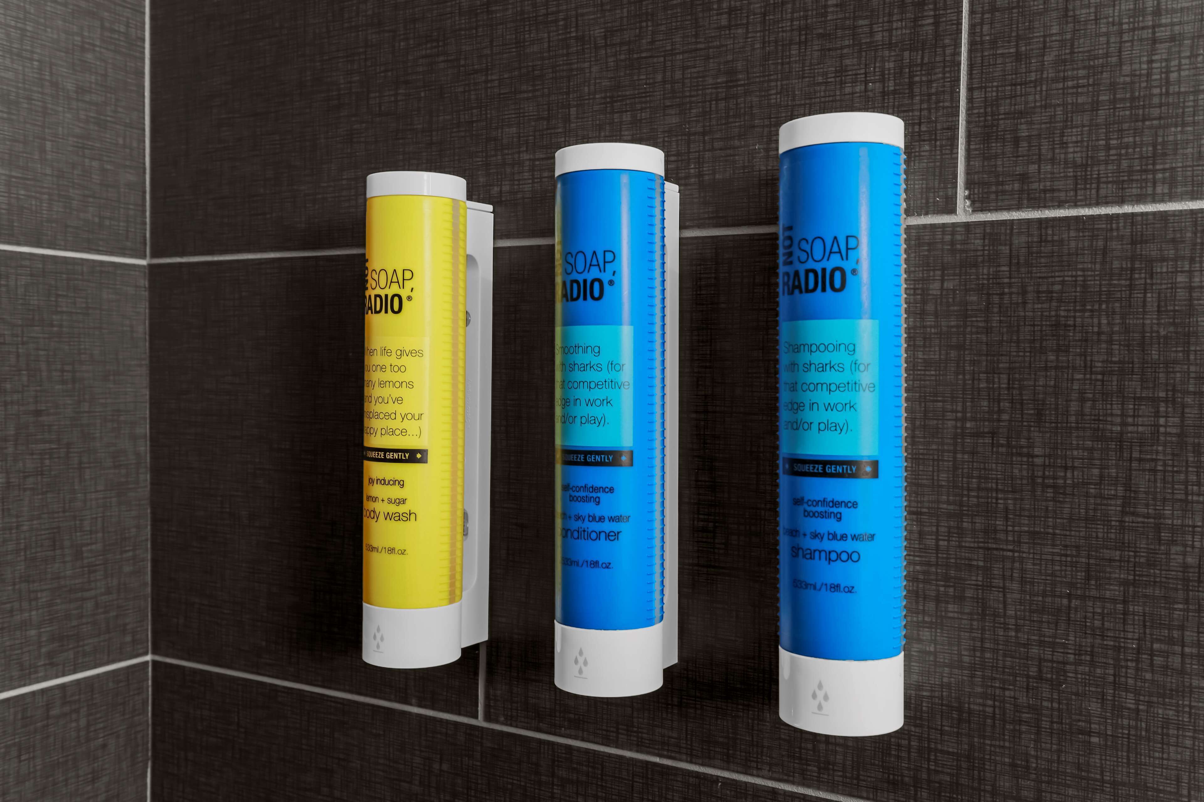 Três frascos de sabonete, rádio e shampoo sobre uma parede de azulejos.