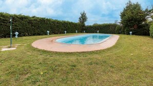 Uma piscina retangular com borda de tijolos, cercada por um gramado e um arbusto.