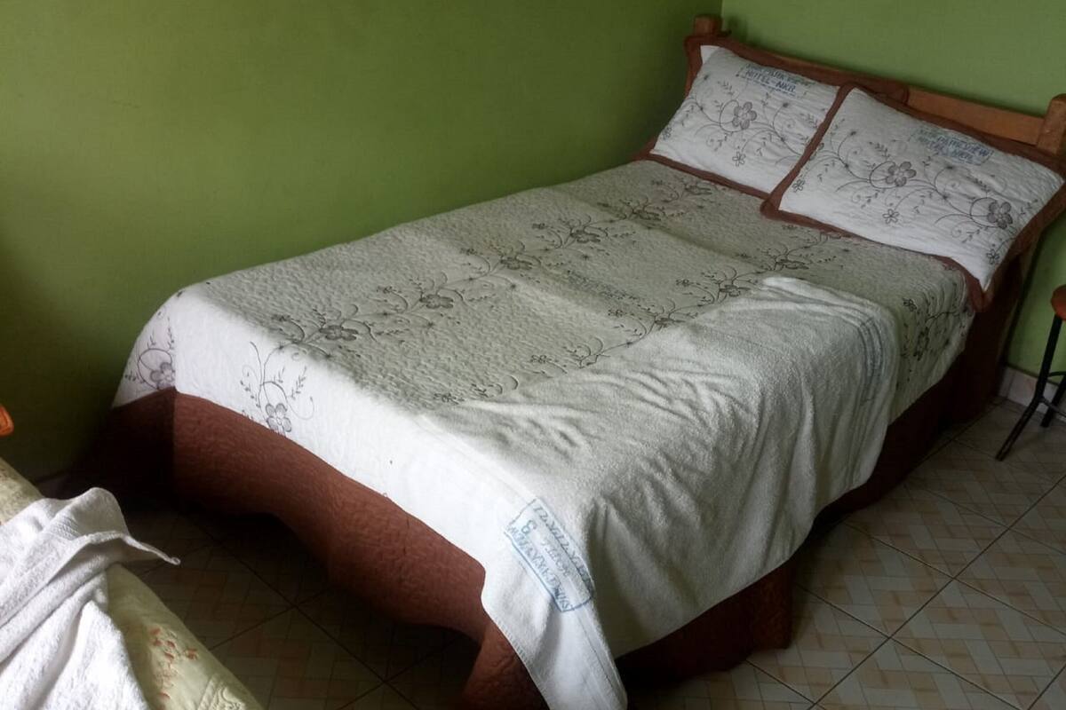 Uma cama de solteiro com colcha florida, cabeceira de madeira e parede verde.