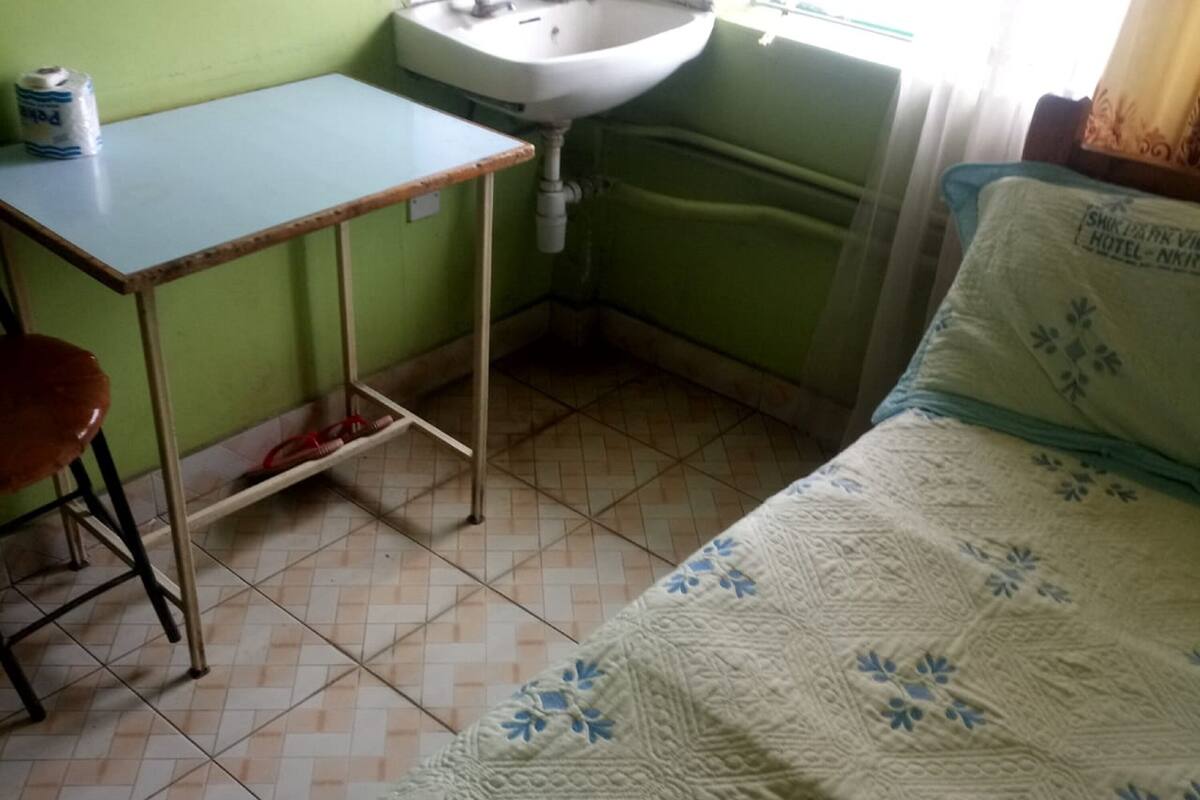 Quarto pequeno com cama, escrivaninha e pia.