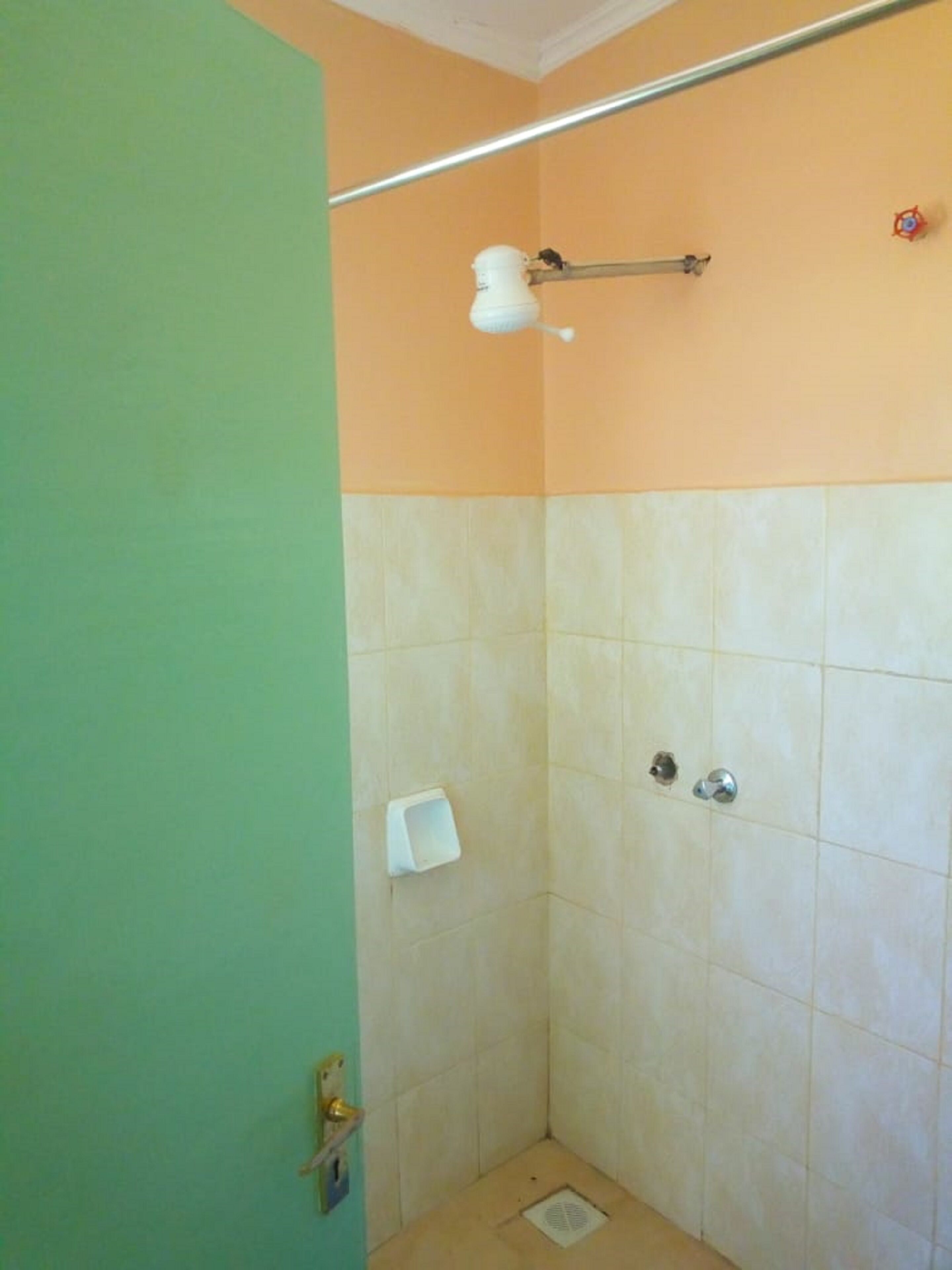 Um banheiro pequeno revestido com azulejos, com chuveiro, porta-toalhas e rolo de papel higiênico.