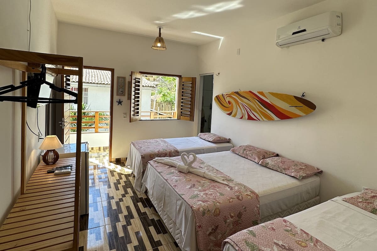 Quarto de hotel com duas camas, um banco de madeira, um abajur e ar condicionado fixado na parede.