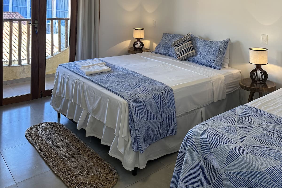 Quarto de hotel com duas camas, varanda e parede decorada com peças de tecido.