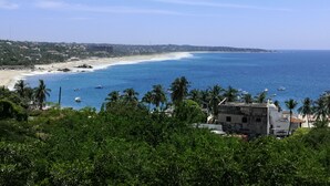 Vista costeira com praia, oceano e um edifício com fachada branca e telhado vermelho.