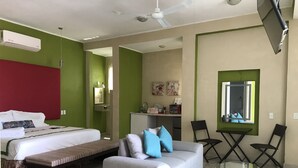 Quarto de hotel moderno com uma cama, um sofá, uma mesa de centro de vidro e uma TV fixada na parede.