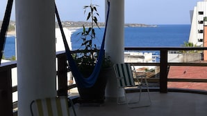 Uma varanda com vista para o mar, uma rede e duas cadeiras.