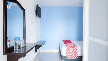 Quarto de hotel com cama, televisão na parede, mesa de cabeceira com espelho e manta vermelha estampada.