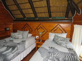 Quarto com duas camas, cada uma com roupa de cama com tema de zebra, paredes de madeira e telhado de palha.
