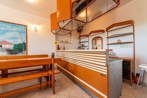 Uma mesa de recepção com um banco de madeira, um quadro de uma casa e prateleiras com diversos objetos.