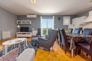 Uma sala de estar moderna com área de jantar, televisão e vista através de uma grande janela.