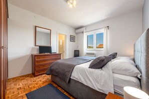 Quarto com cama, penteadeira, televisão, janela e radiador.