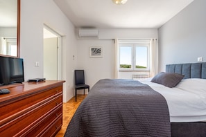 Quarto com cama, penteadeira, televisão, cadeira e janela com vista.