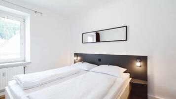 Quarto moderno com cama grande, janela e espelho fixado na parede.