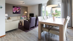 Uma sala de estar moderna com sofá, uma mesa de jantar com cadeiras, TV e uma janela grande com cortinas.