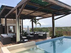 Área externa coberta com piscina, assentos e vista da cidade.