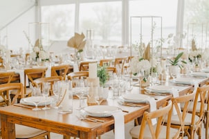 Uma sala de banquetes com mesas montadas para um evento formal, com toalhas brancas, copos de cristal e arranjos florais.