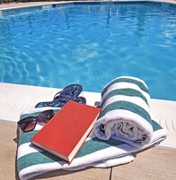 Uma área à beira da piscina com uma toalha, um livro e um par de óculos de sol.