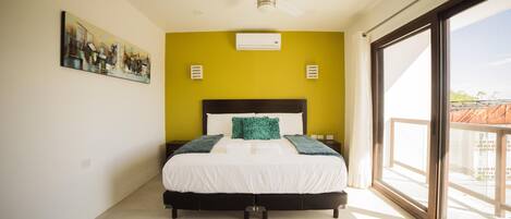 Quarto com cama, ventoinha no teto, ar condicionado, janela e um quadro na parede.
