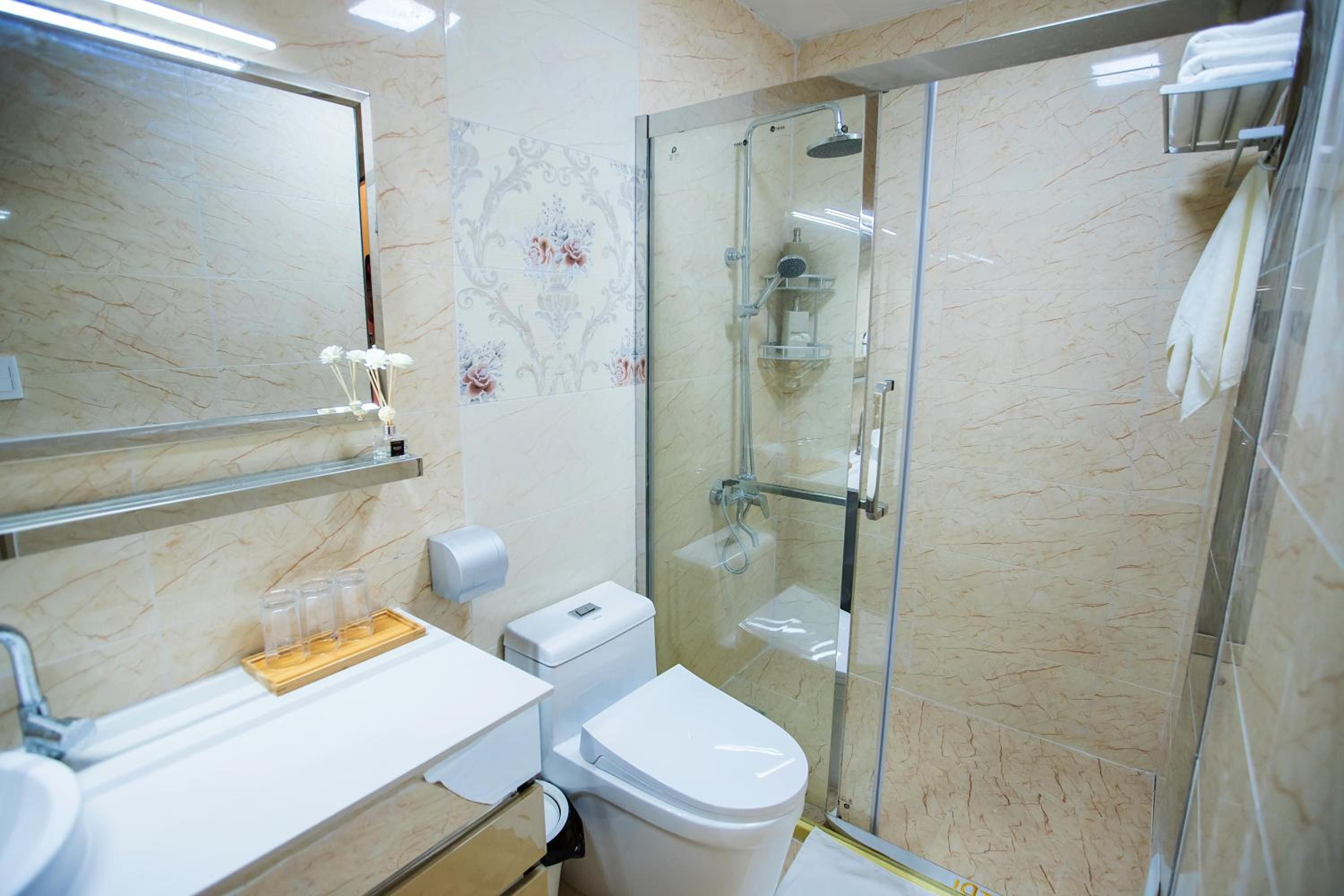 Casa de banho moderna com chuveiro separado por vidro, sanita, lavatório com espelho e porta-toalhas.