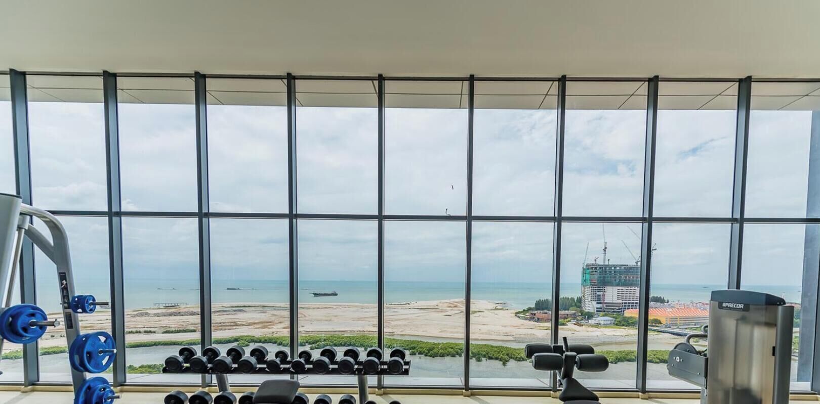 Academia com vista para a praia e um canteiro de obras, visíveis através de grandes janelas.