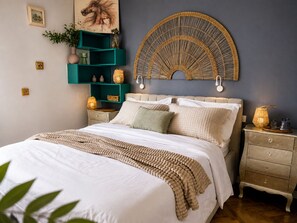Quarto com cama, mesa de cabeceira, prateleira na parede e uma obra de arte.