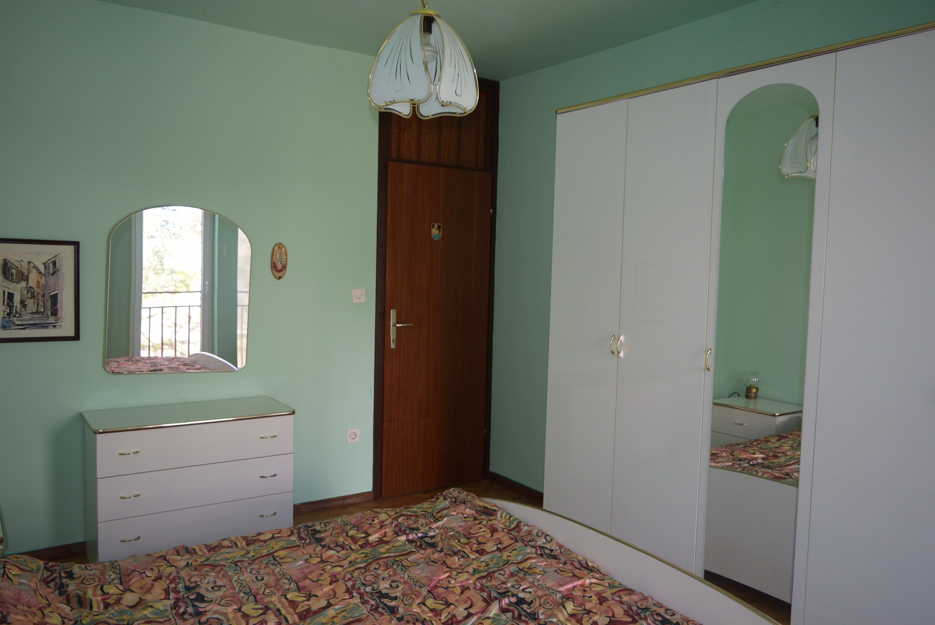 Quarto com cama, penteadeira, guarda-roupa, espelho e luminária no teto.