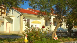 Uma casa com telhado de telhas vermelhas, um guarda-sol listrado em amarelo e branco e uma estátua de gnomo.