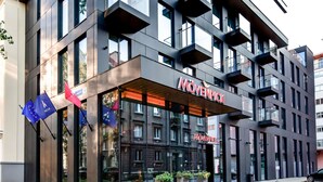 Um hotel moderno com um letreiro de 'Mövenpick' em destaque, janelas amplas e bandeiras.