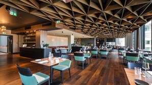 Um restaurante moderno com design geométrico no teto, piso de madeira e diferentes opções de assentos.
