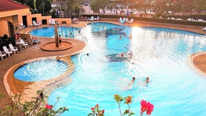 Uma grande piscina interior com várias pistas de natação, rodeada por espreguiçadeiras e uma pequena área ajardinada.
