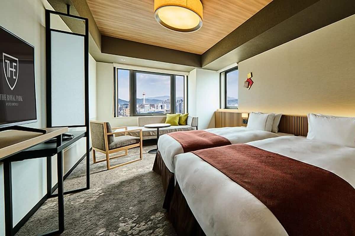 Quarto de hotel com duas camas, uma escrivaninha, uma cadeira, uma mesa pequena e vista para a cidade.