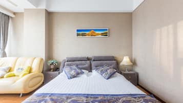 Quarto de hotel com uma cama grande, um sofá, uma mesa de cabeceira com abajur e um quadro na parede.
