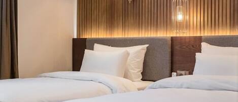 Quarto de hotel com uma cama grande, cabeceira de madeira e luminária fixada na parede.