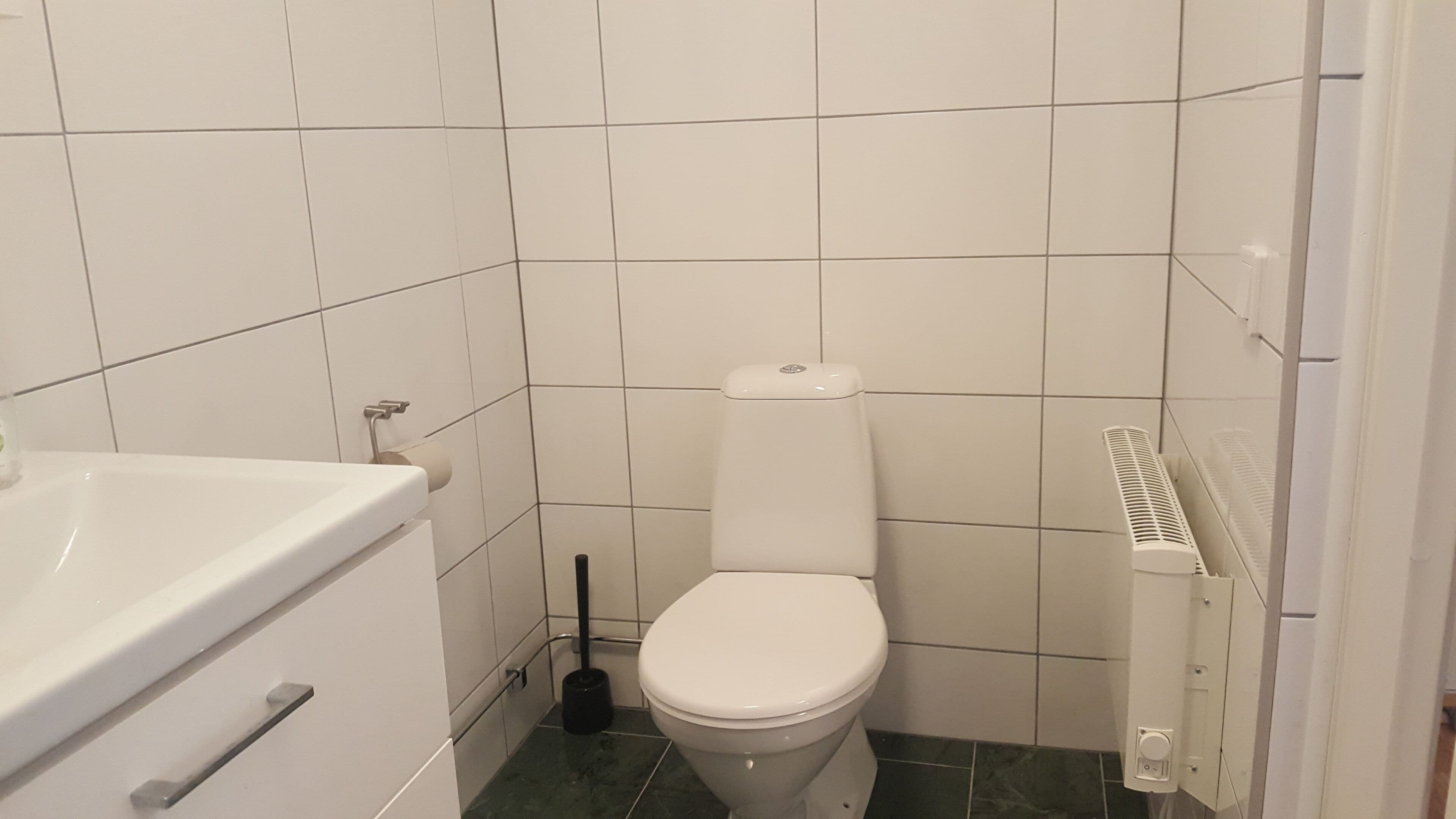Casa de banho pequena e branca, com sanita, lavatório branco e unidade de ventilação.