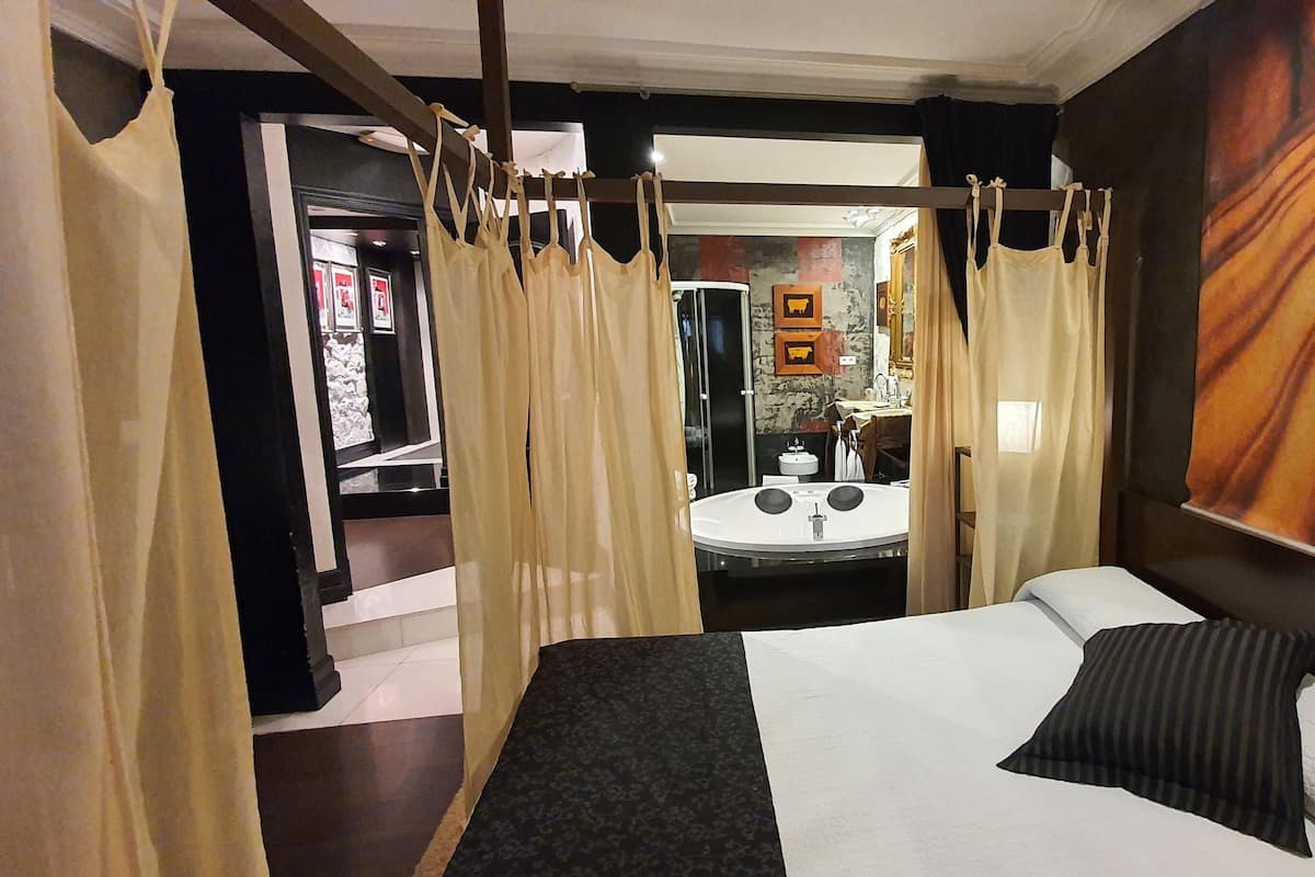 Quarto de hotel com uma cama, uma mesa redonda e um espelho.