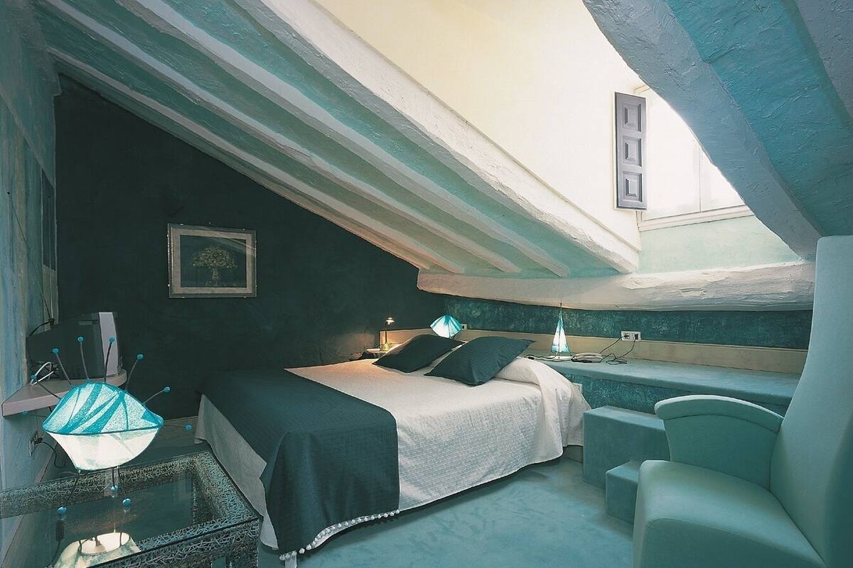 Um quarto com cama, mesa de cabeceira, abajur e uma cadeira.