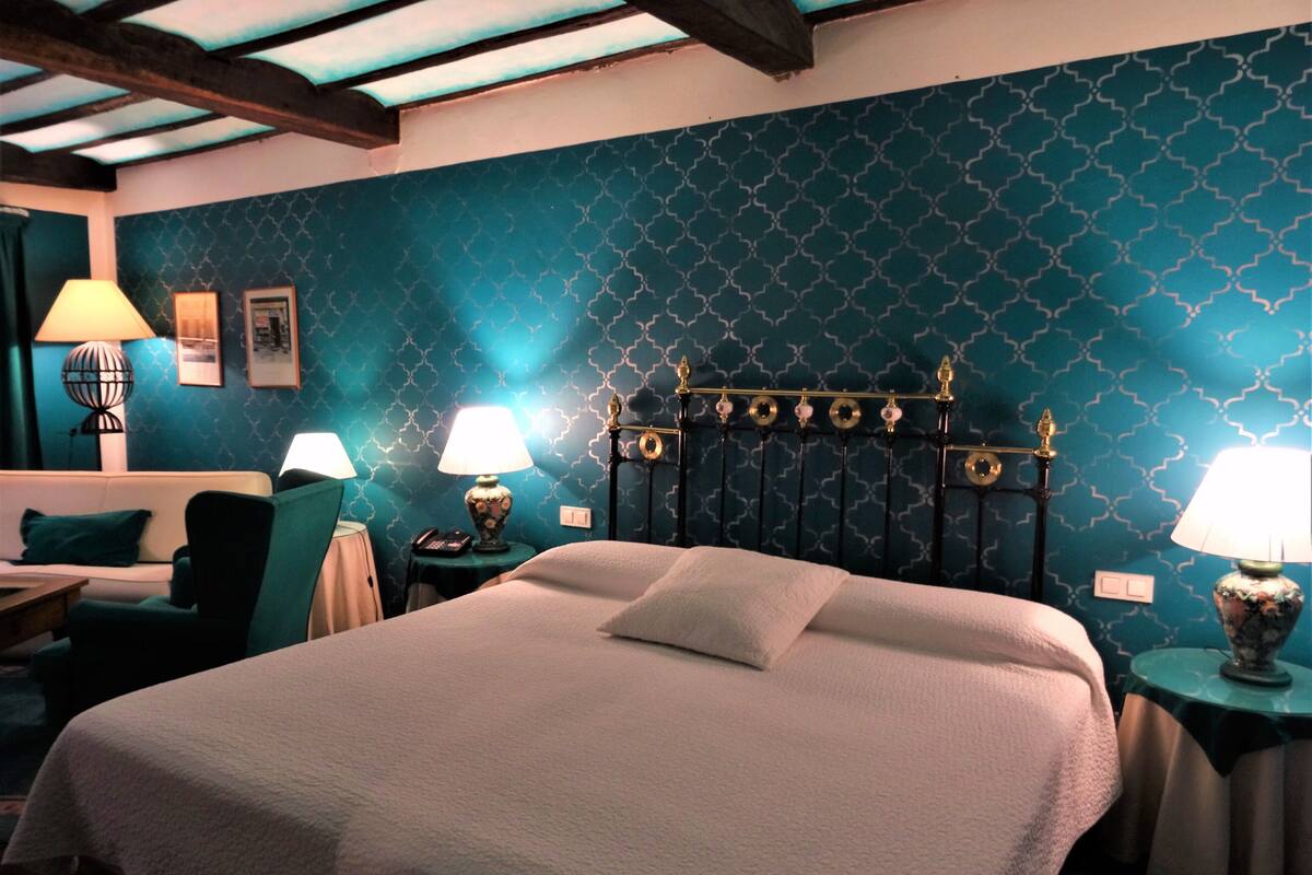 Quarto de hotel com uma cama grande, duas mesas de cabeceira com luminárias, uma cadeira e uma pequena mesa.