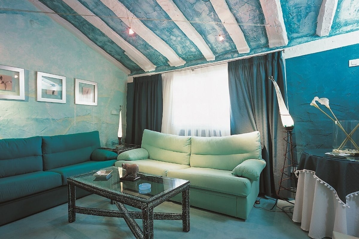 Sala de estar com sofá verde, mesa de centro de vidro e uma luminária.