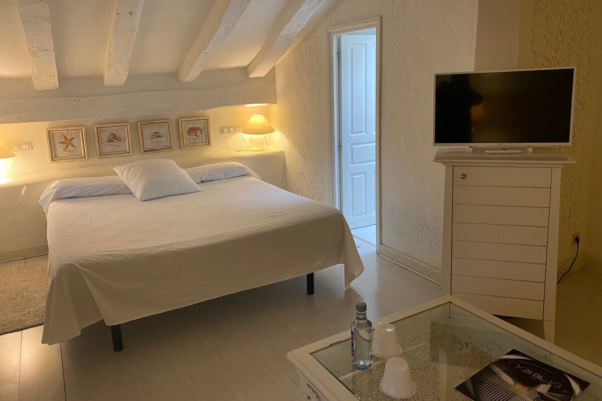 Um quarto com uma cama, uma televisão sobre um móvel e uma porta que dá para uma varanda.