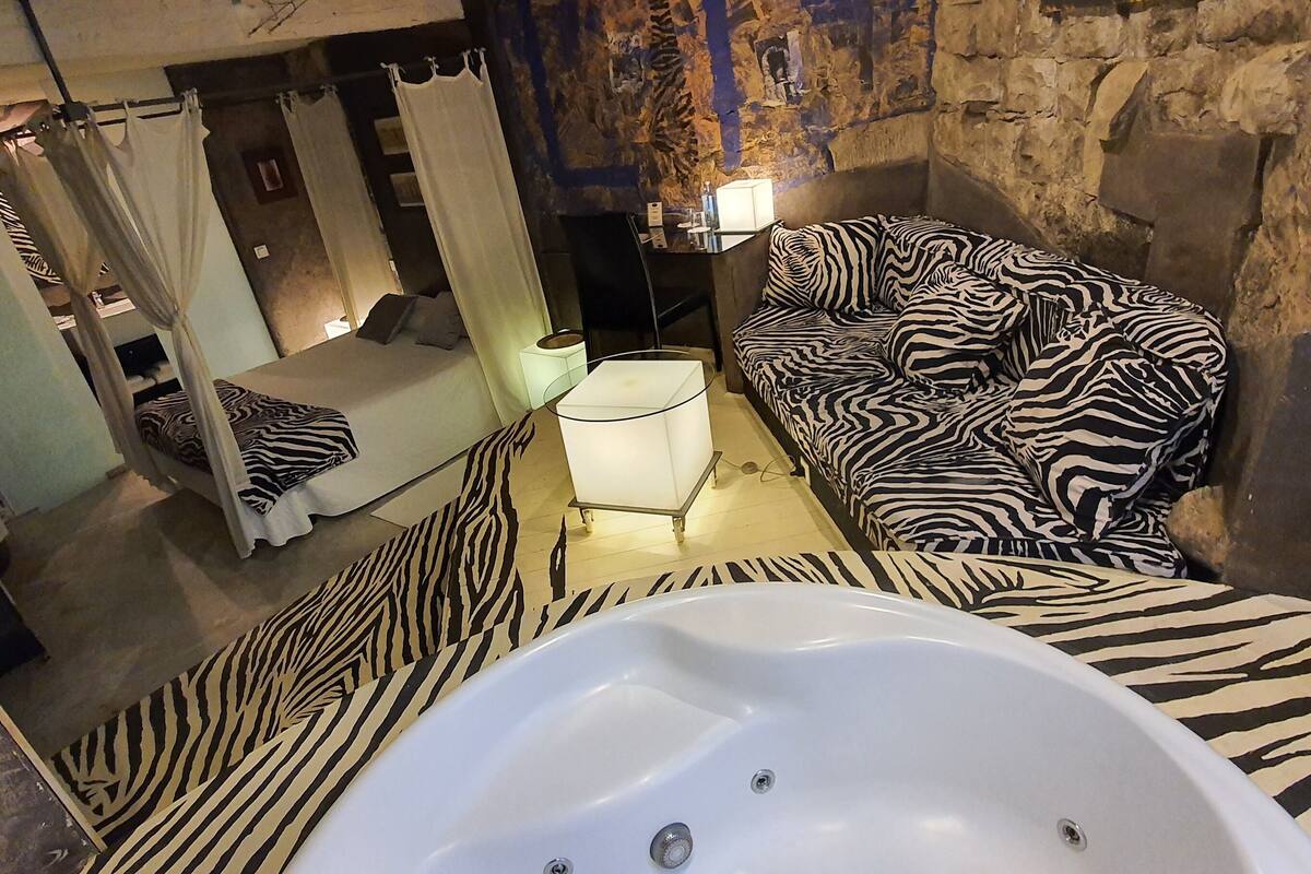 Um banheiro com banheira estampada em zebra, cama com dossel e sofá com padrão de zebra.