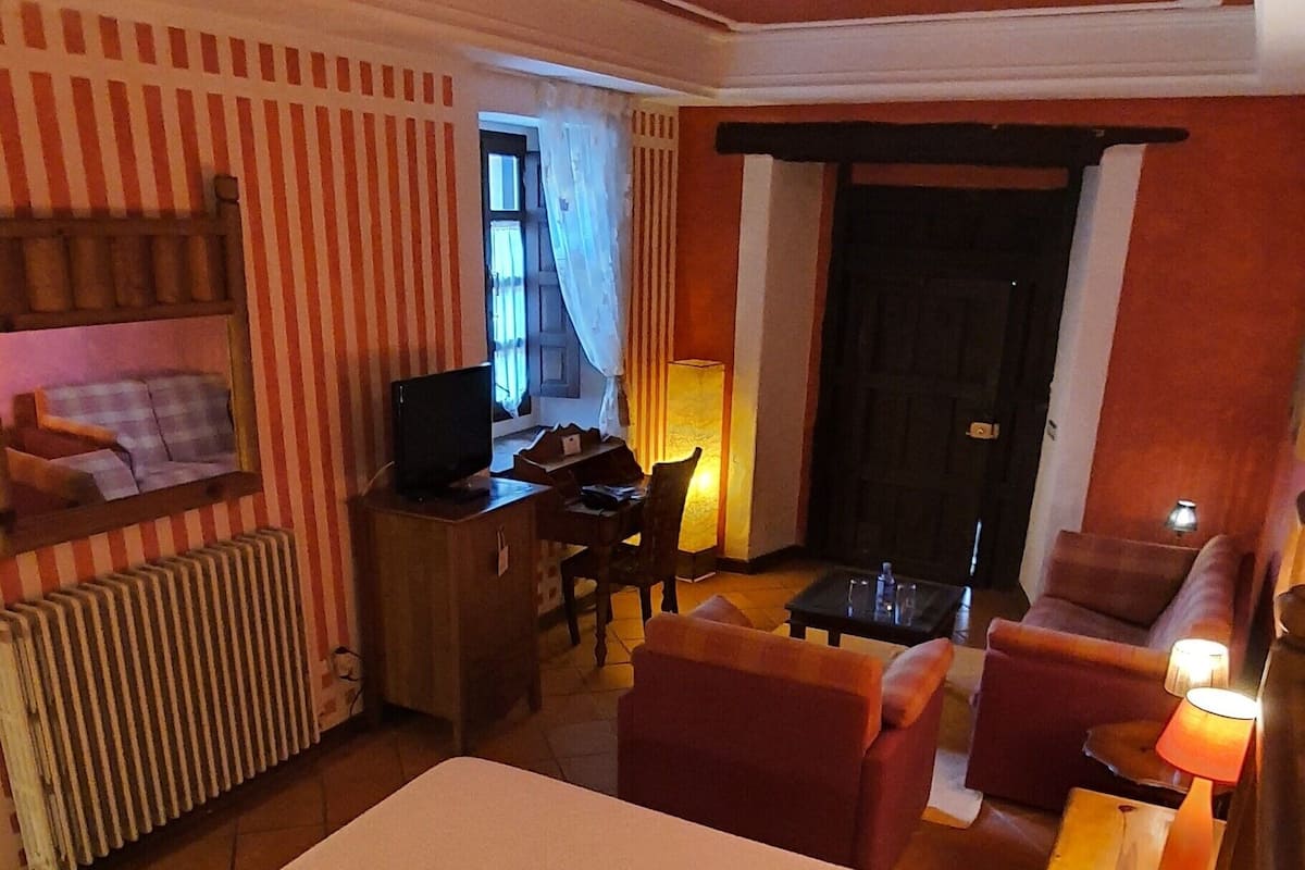Quarto de hotel com uma cama grande, uma escrivaninha com computador, uma cadeira e janela com cortinas.